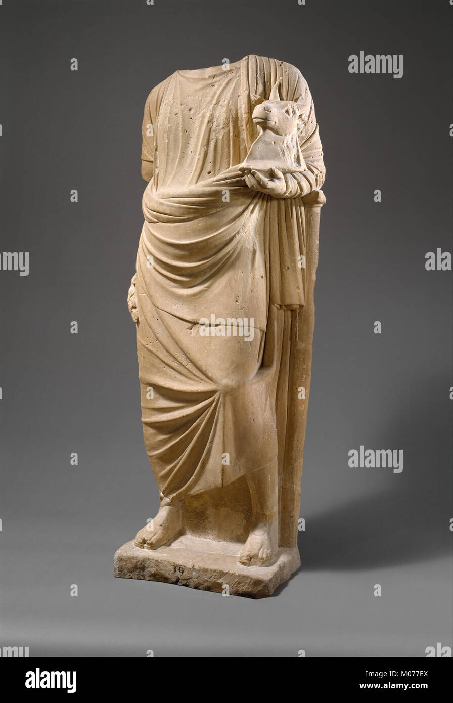 This limestone statue depicts a man holding a bull's head mask, an ...