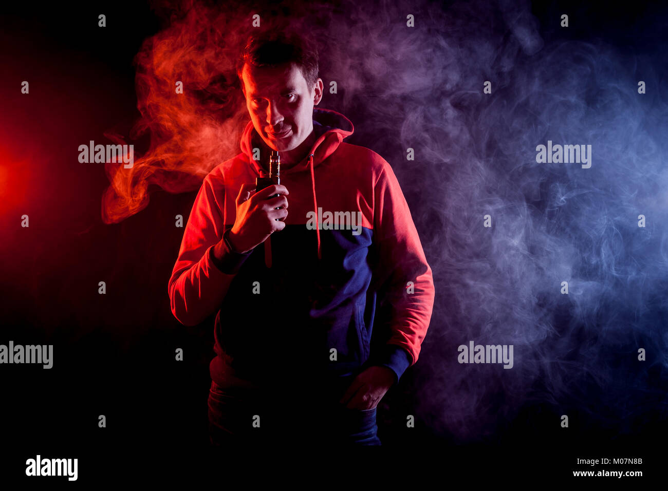 Man in sport hoody vaping an electronic cigarette.Isolated on black ...