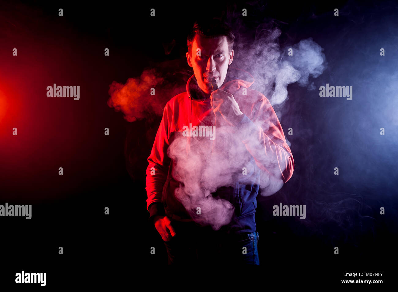Man in sport hoody vaping an electronic cigarette.Isolated on black ...