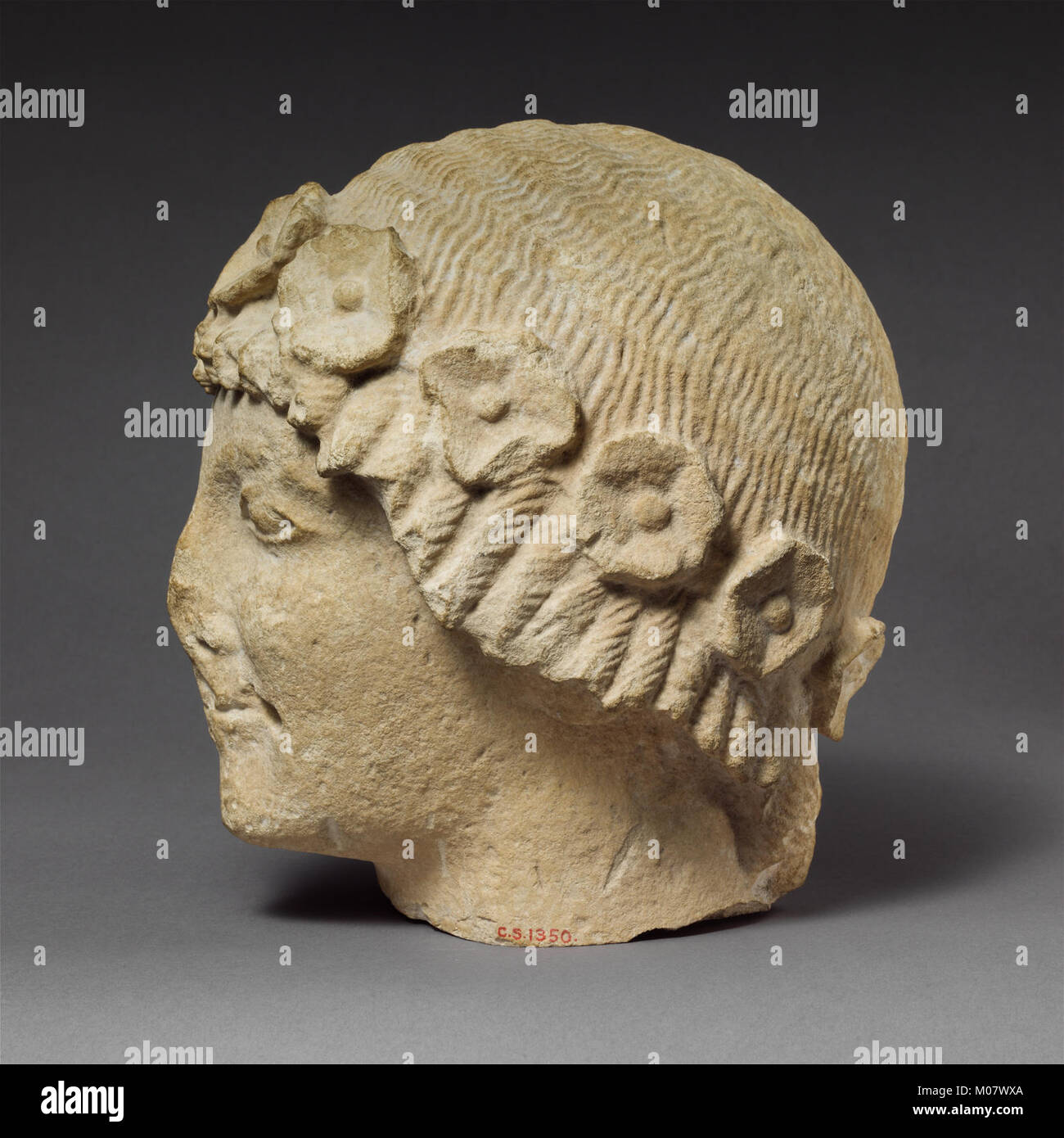 A limestone sculpture of a beardless male head adorned with a wreath of ...