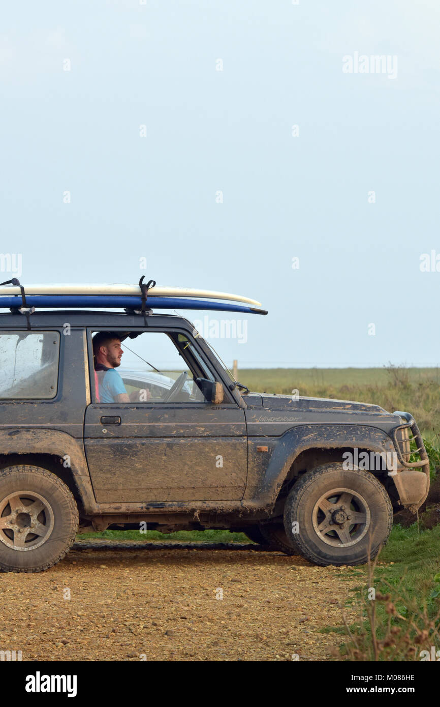 a surfer in an old muddy jeep or four wheel drive vehicle waiting for a ...