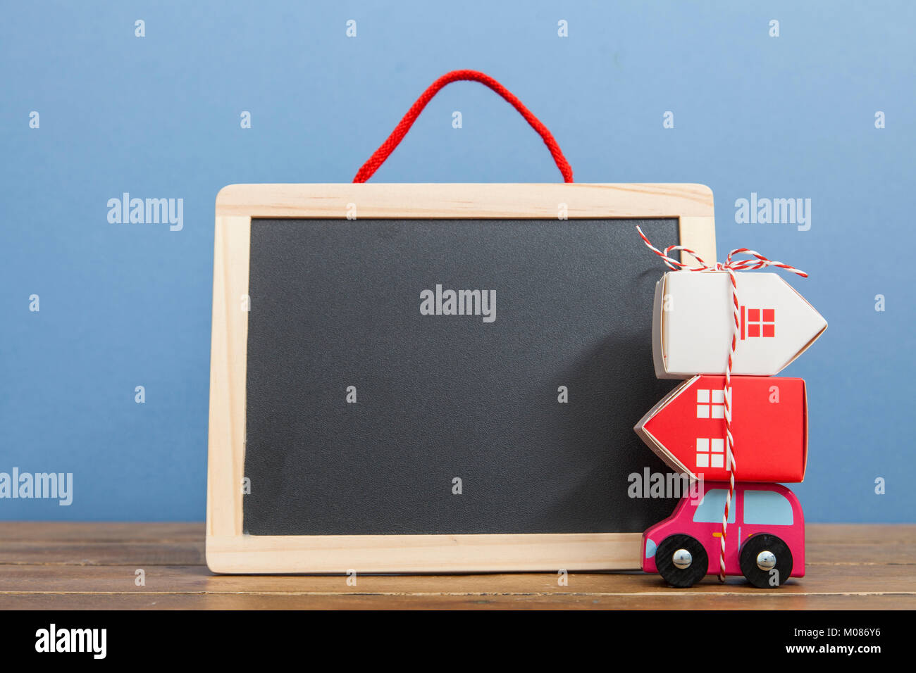 Toy car carrying a stack of houses next to a blank blackboard. Moving ...