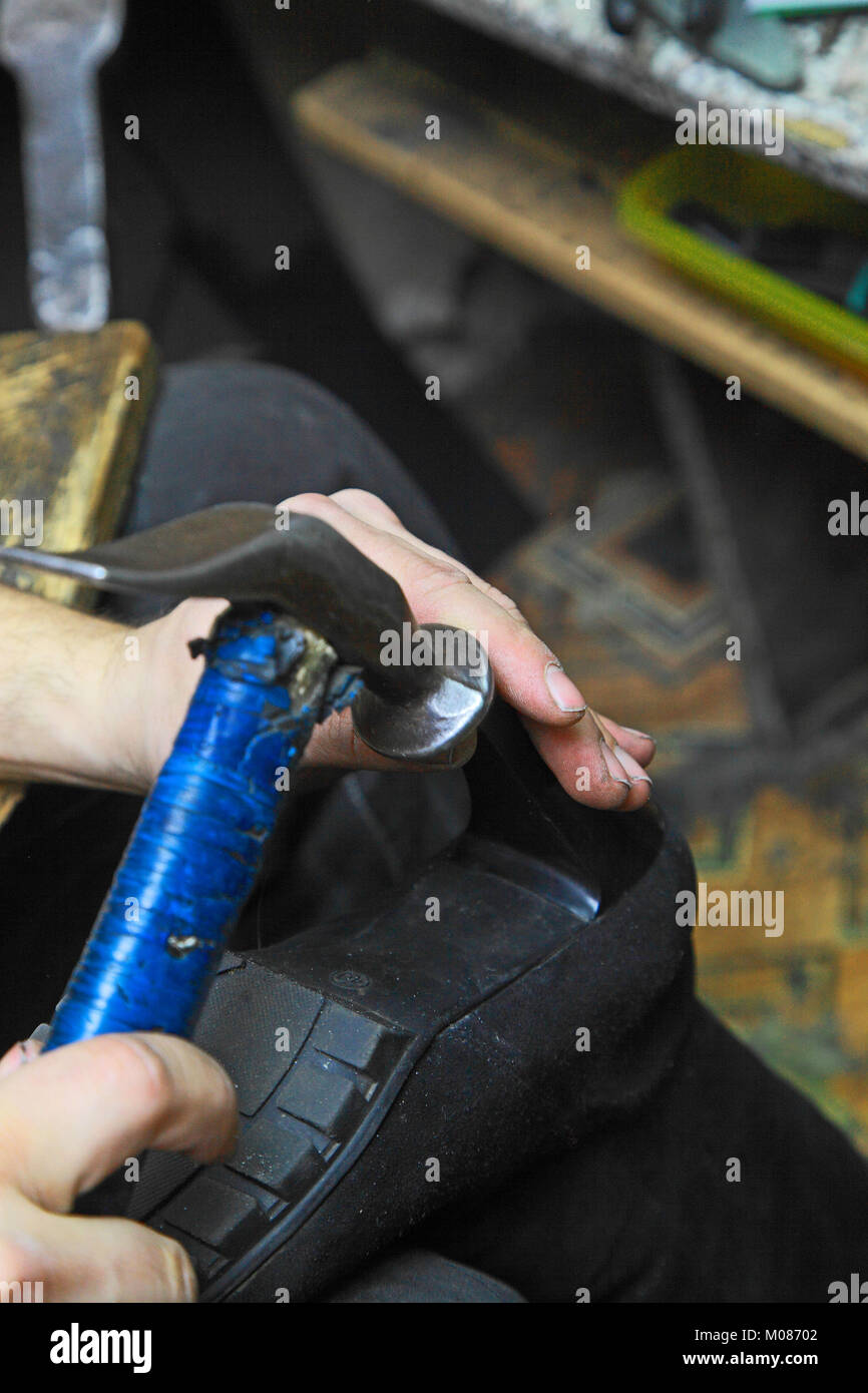 male hands of the shoemaker hammer in a nail with a hammer into the ...