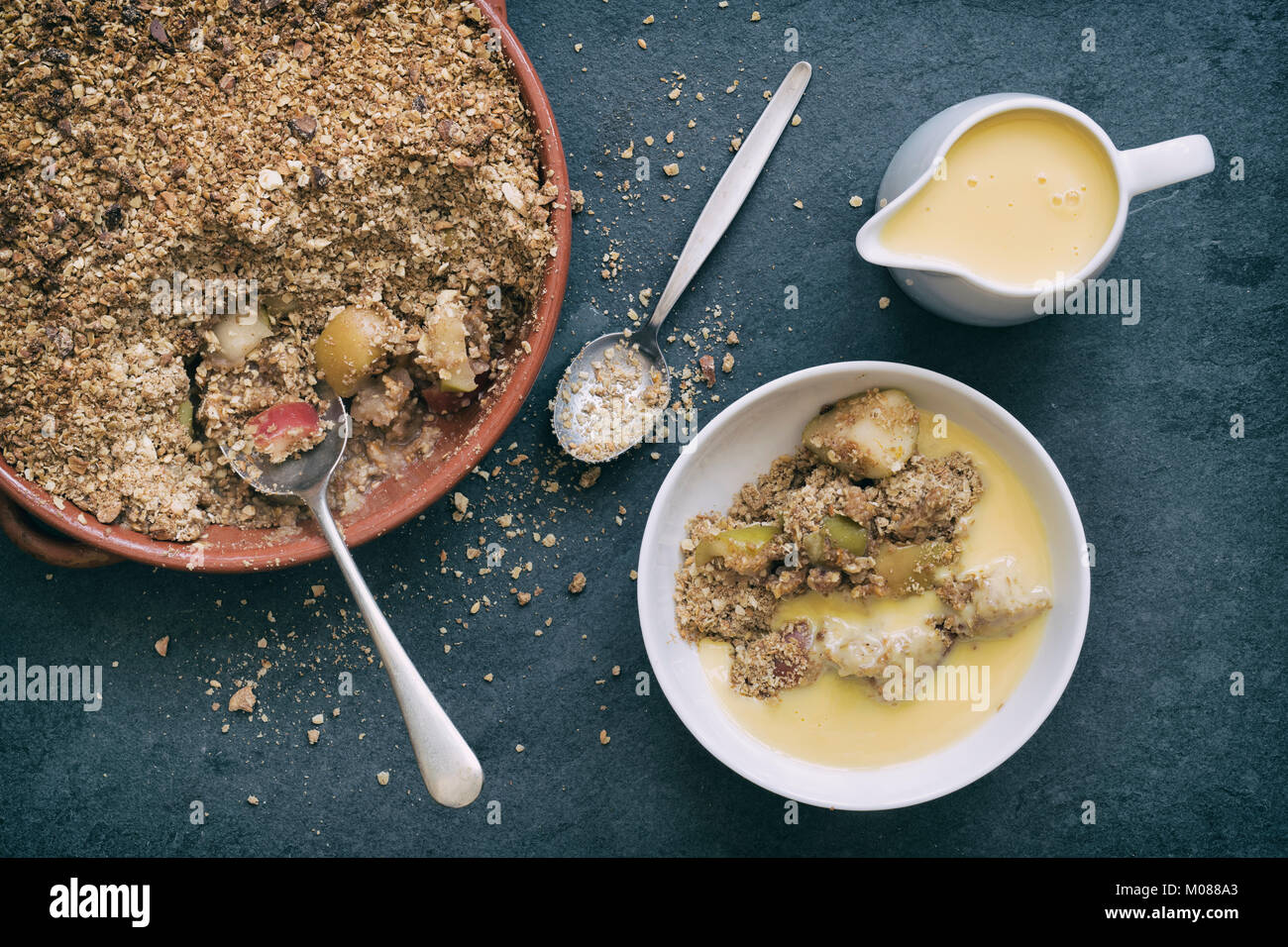 Apple crumble and custard on a slate background Stock Photo - Alamy