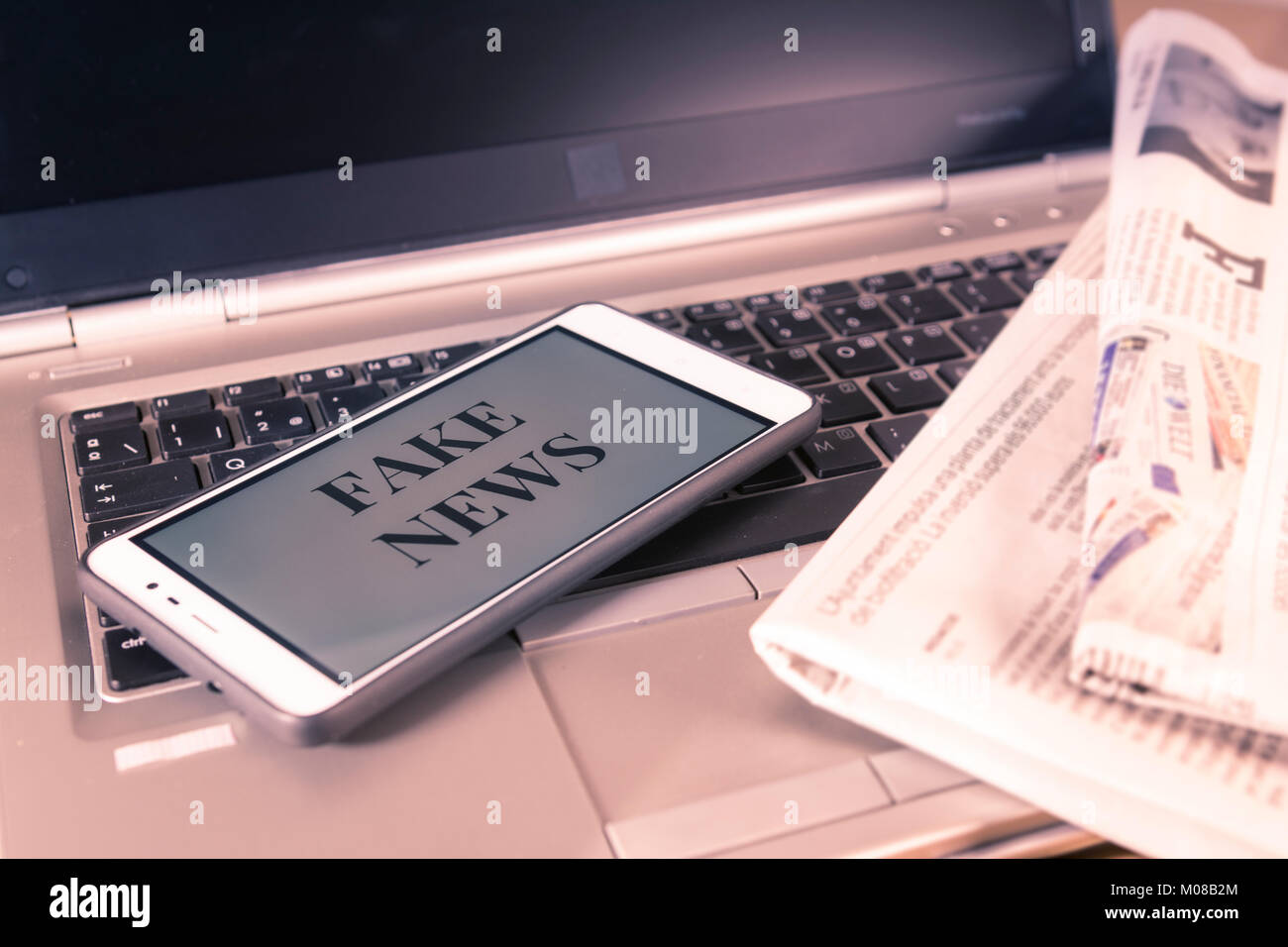 Smartphone with Fake News words on screen over a newspaper and a laptop ...