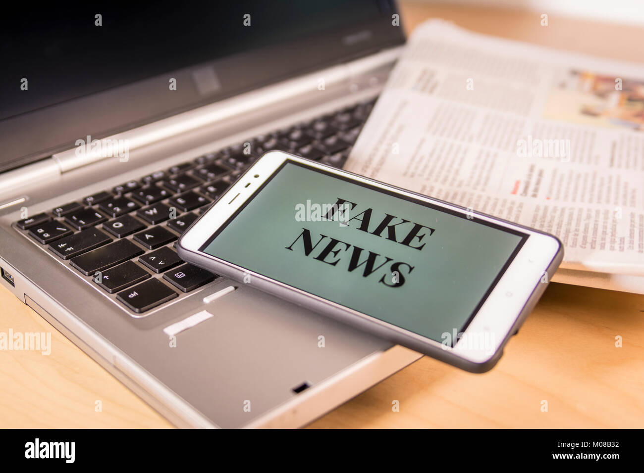 Smartphone with Fake News words on screen over a newspaper and a laptop ...