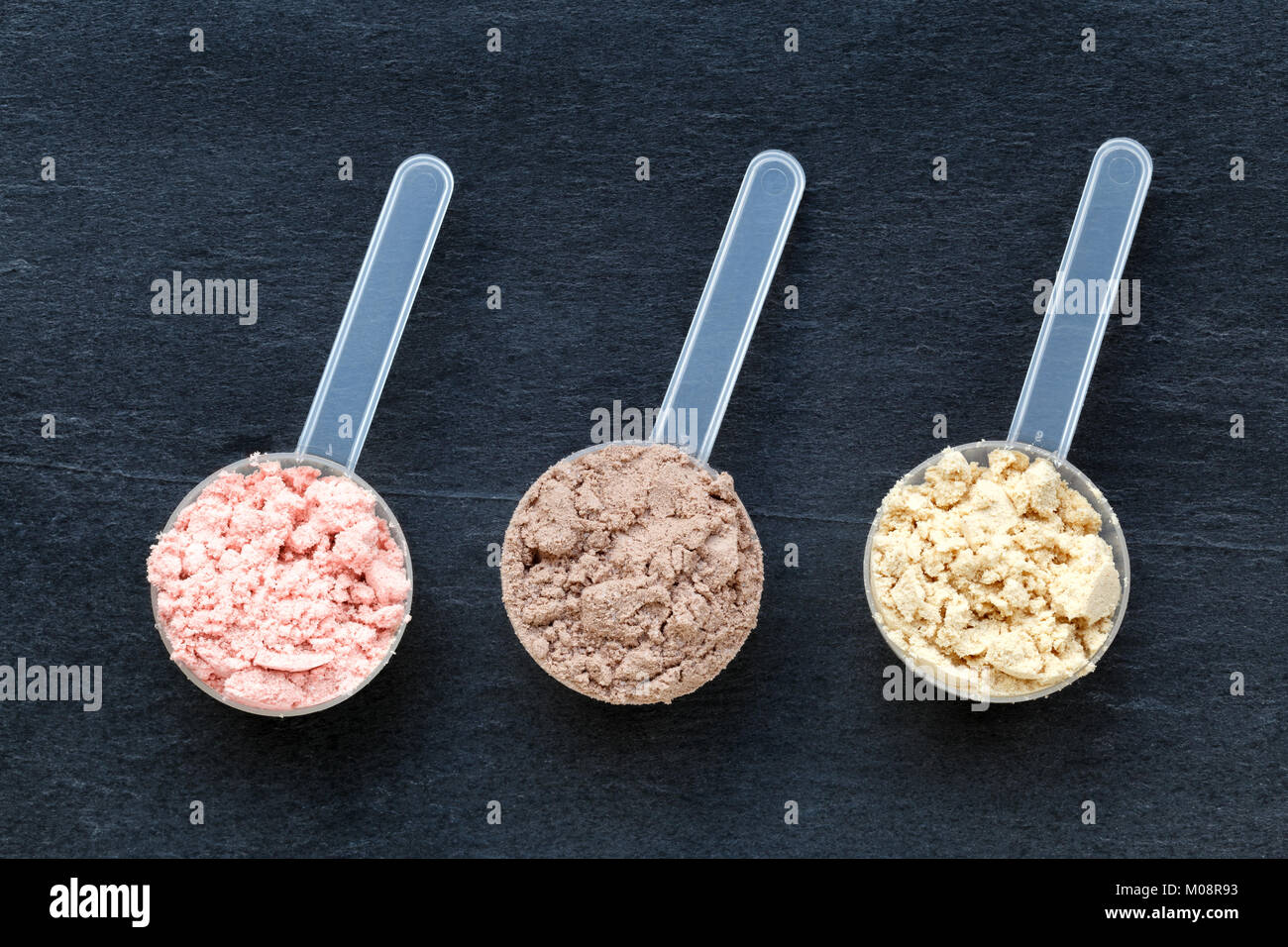 Plastic measuring spoons filled with whey protein powder against dark ...