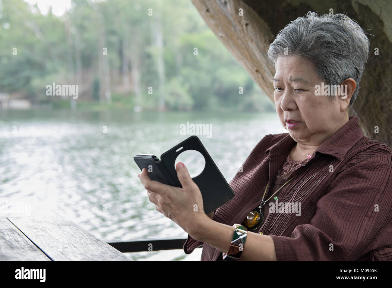 asian elder woman holding mobile phone in garden. elderly female ...