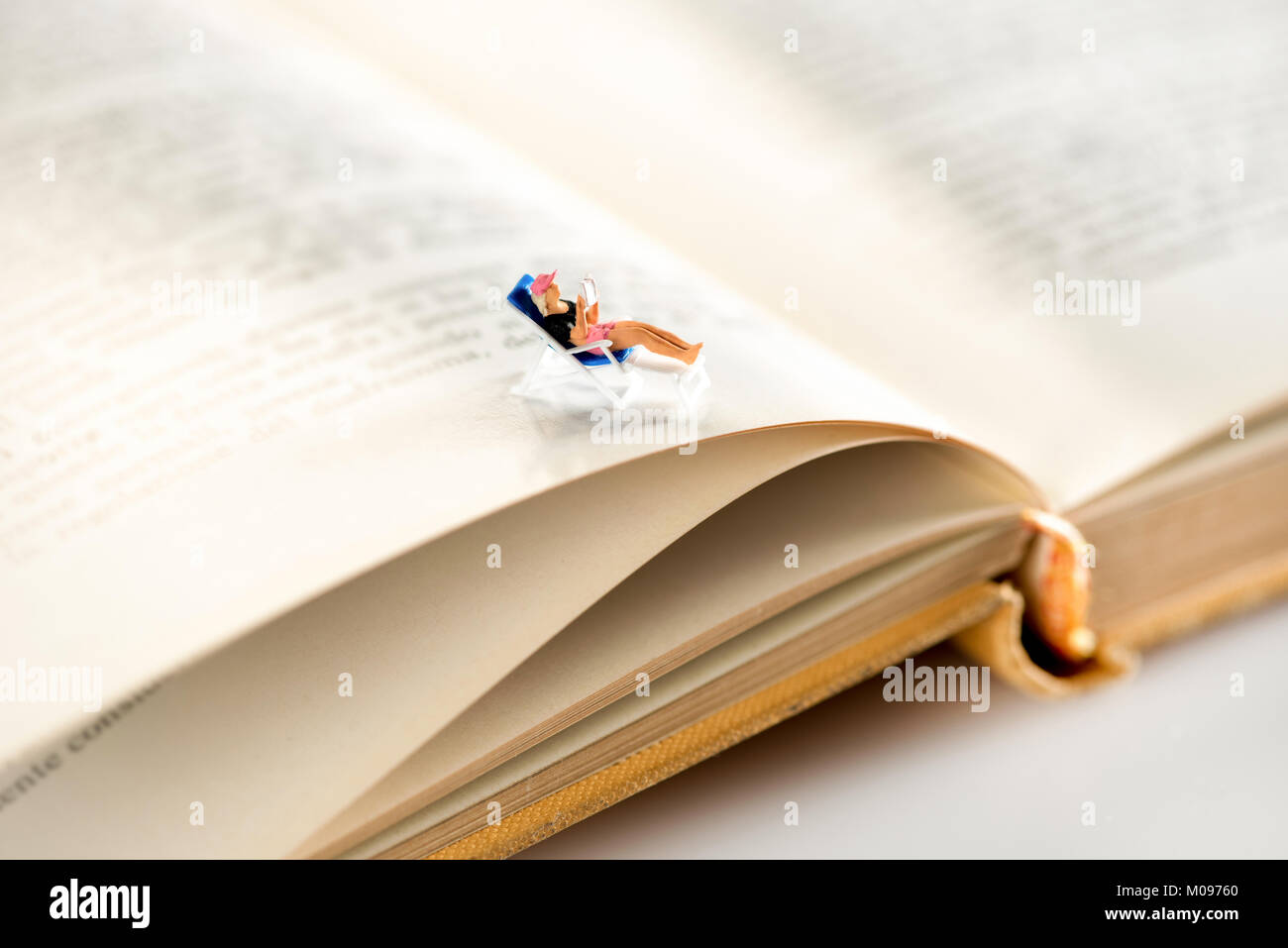 Conceptual close-up of a miniature figure woman reading a book on a ...