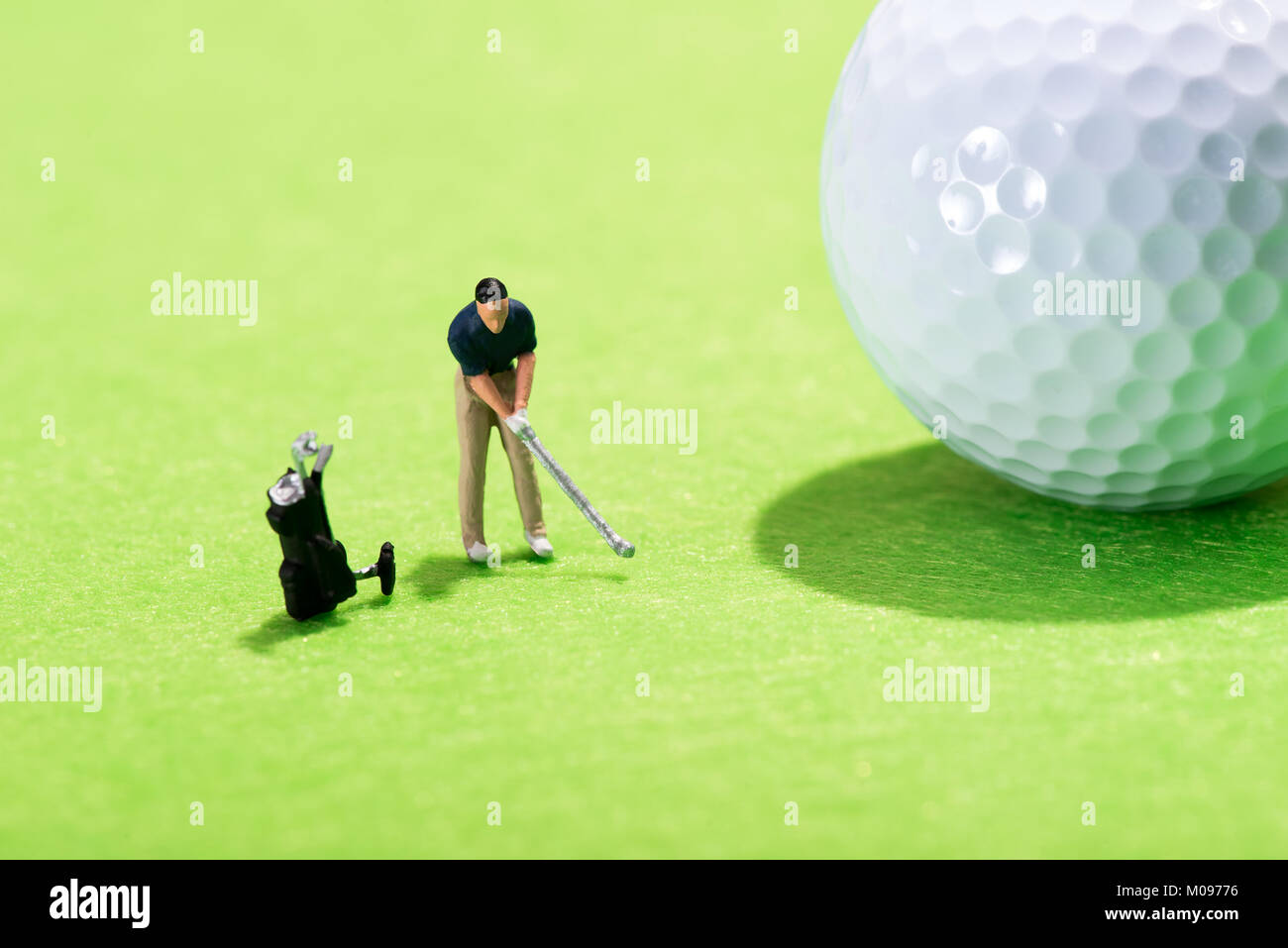 Miniature figure of a golfer playing a stroke with his golf bag behind ...