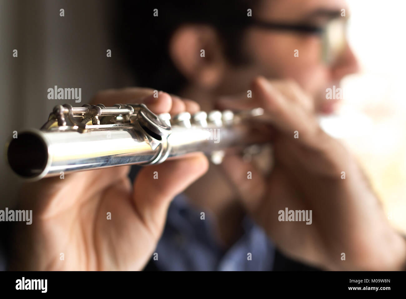 A male flutist playing a silver transverse flute indoors, profile view ...