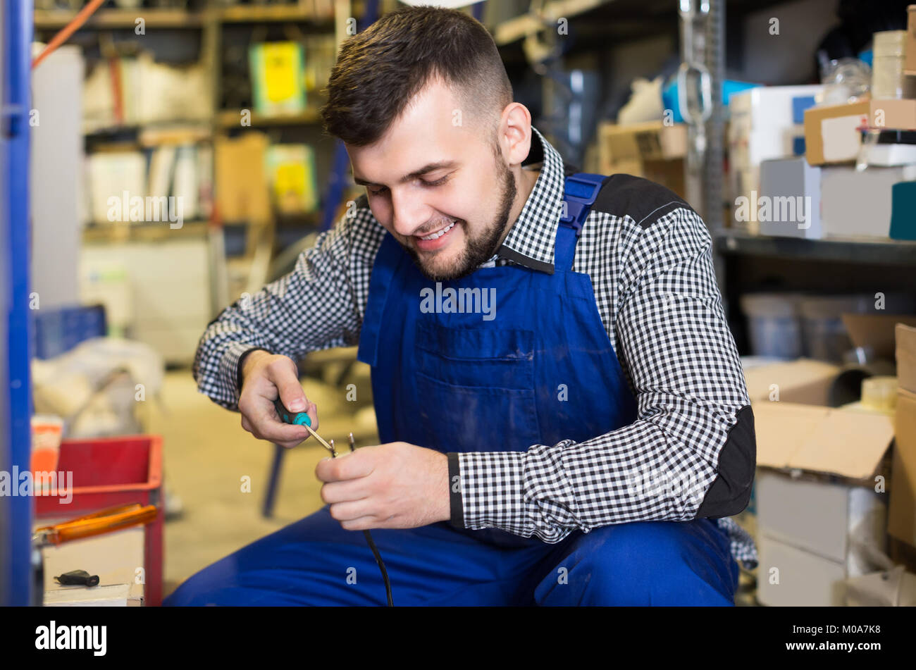 Production worker in uniform working with tools for fixing adaptor plug ...