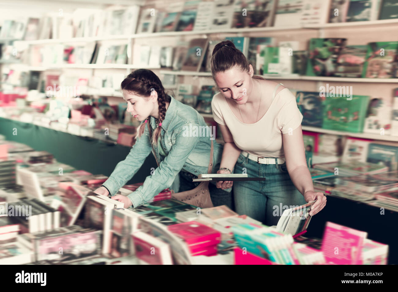 Positive woman with girl buying books in bookstore Stock Photo - Alamy