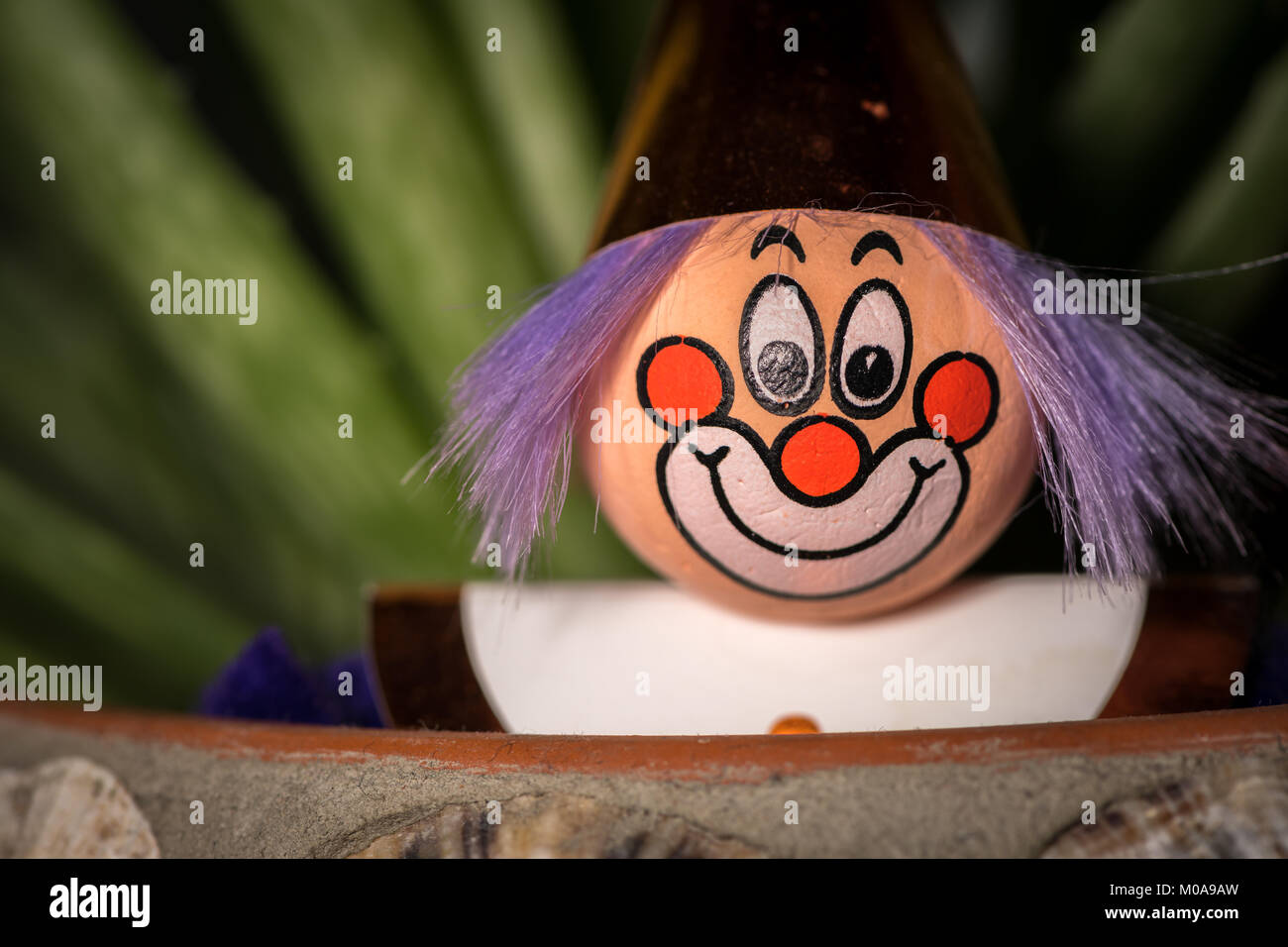 Portrait of a figurine of a clown with a smiling face stuck in a flower ...
