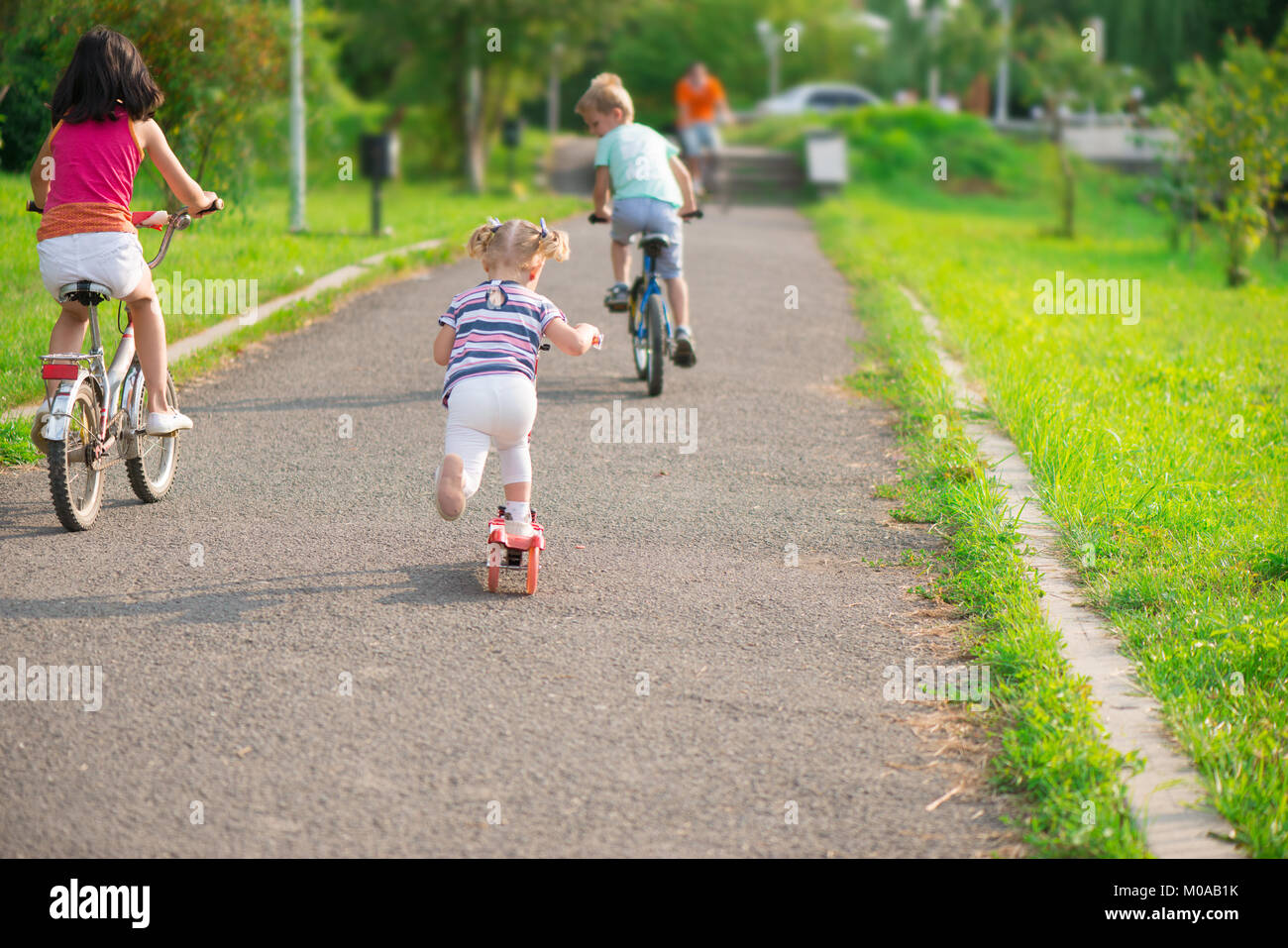 Three happy children riding on bicycle and acooter Stock Photo - Alamy