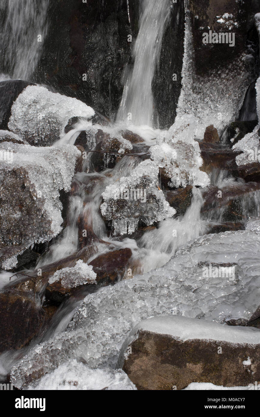Cold winter day. Waterfall with blurred water flow, rocks in a creek or ...
