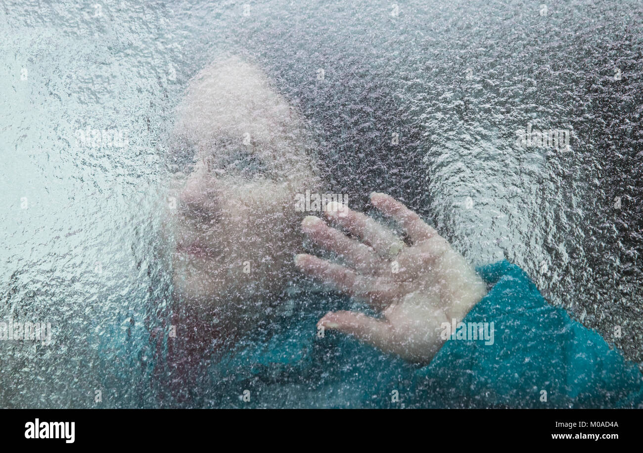 Woman looking through a window covered with thick, textured ice, with ...