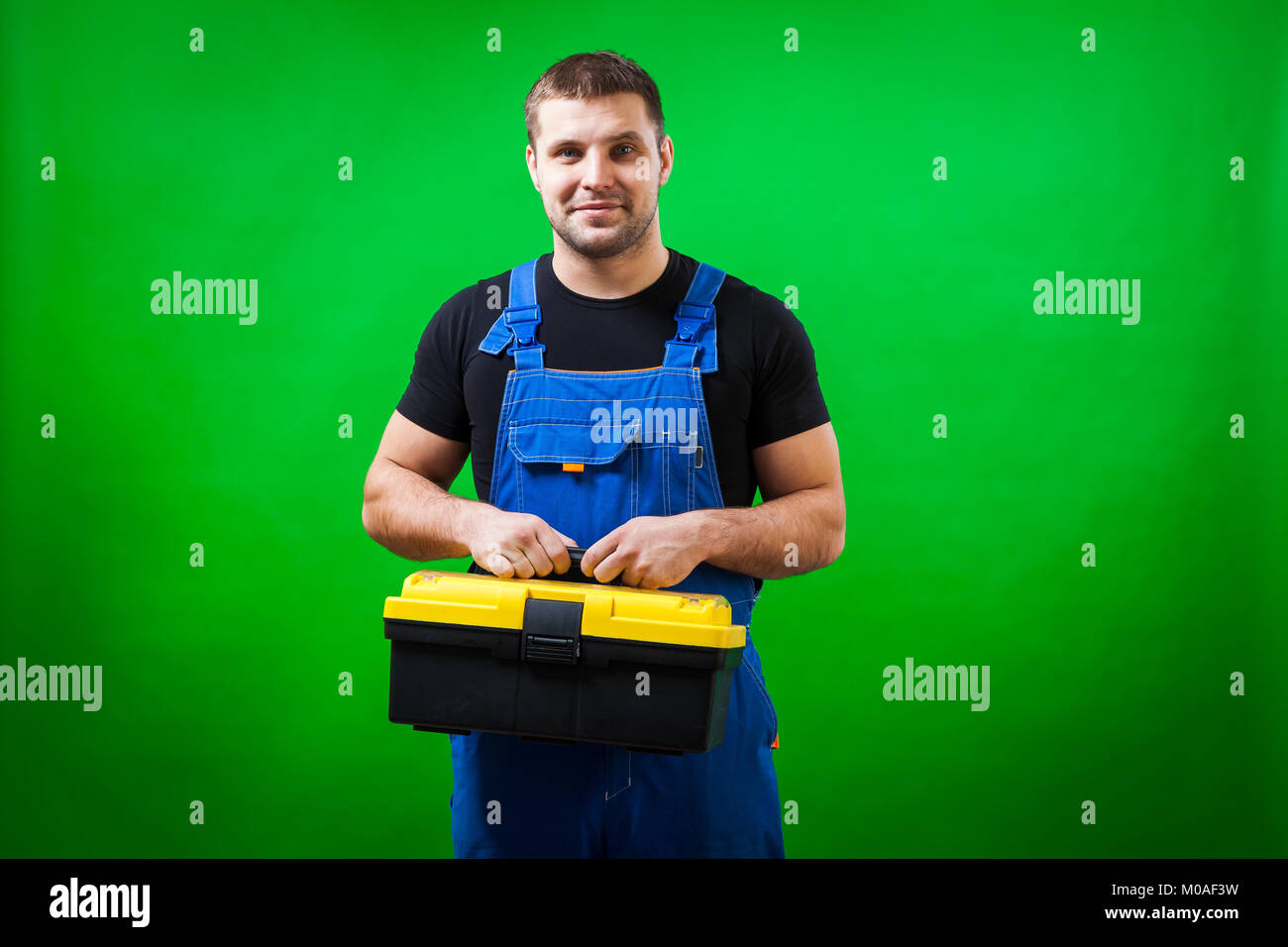 A strong man carpenter in a black T-shirt and blue construction ...