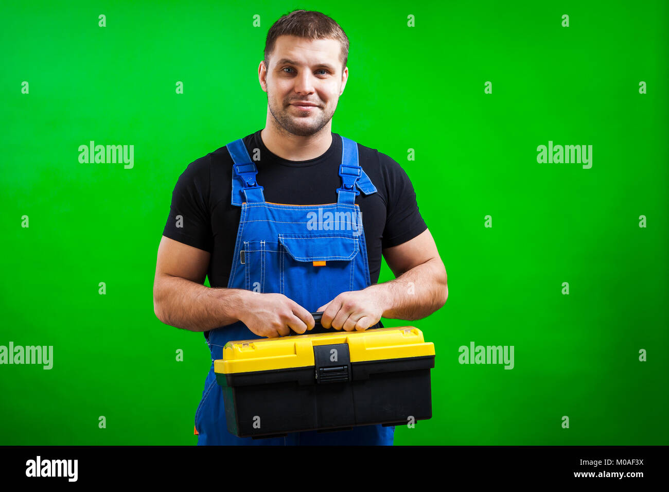 A strong man carpenter in a black T-shirt and blue construction ...