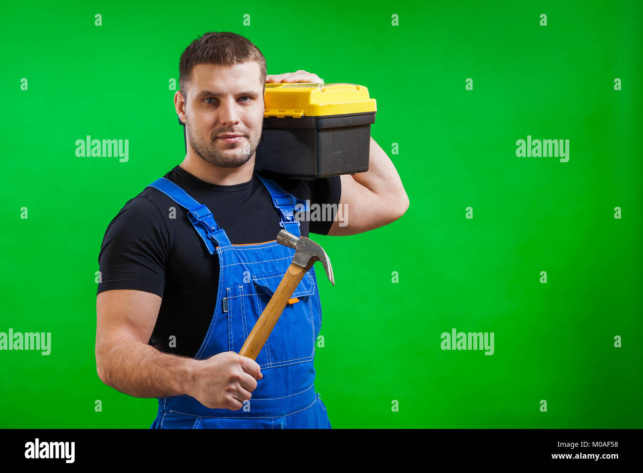 A strong man builder in a black T-shirt and blue construction jumpsuit ...