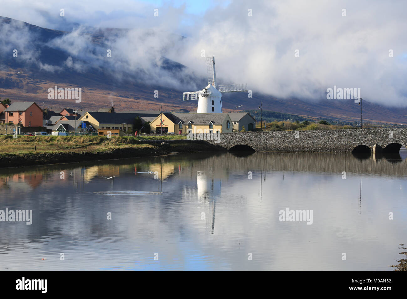 old windmill standing on river estuary with mountain background ...