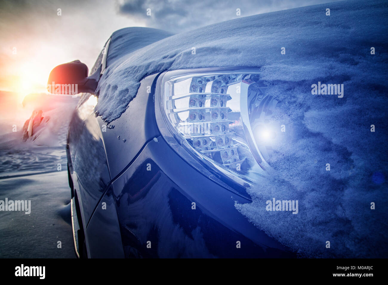 the front of the car with the snow-covered headlight and the sunset of ...