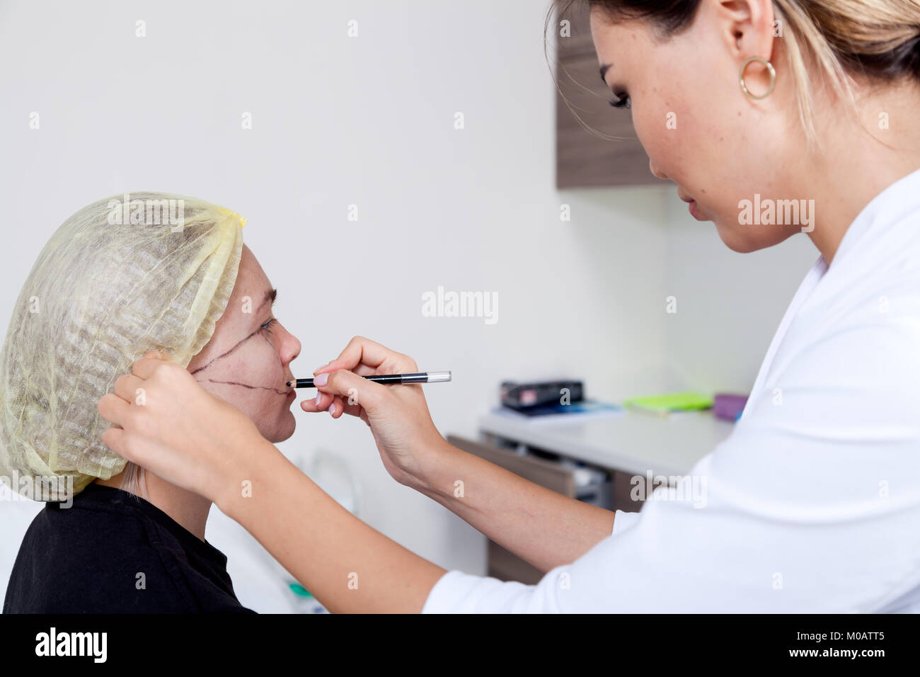 Young female plastic surgeon doing the marking on the face of the woman ...