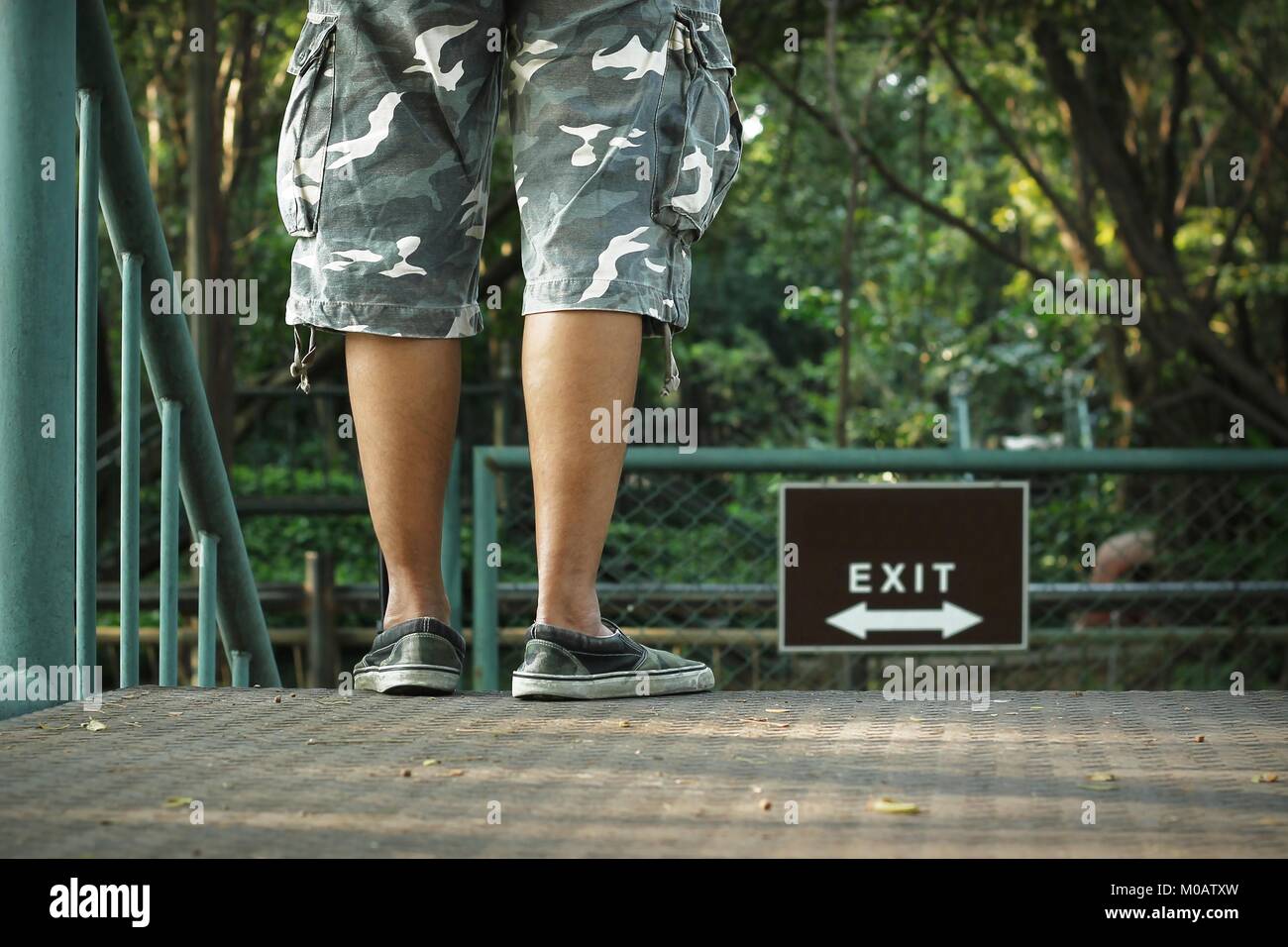 Young man standing on walkway and blur exit sign Stock Photo - Alamy