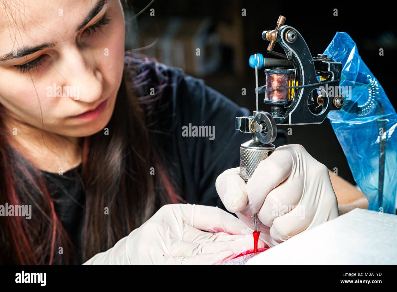 Close up tattoo artist demonstrates the process of getting red tattoo ...