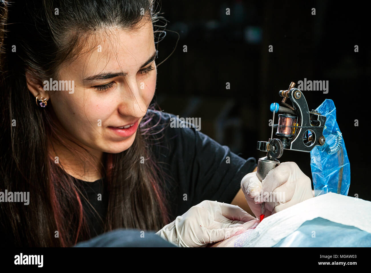 Professional tattoo artist woman makes a tattoo on a young girl's femur ...