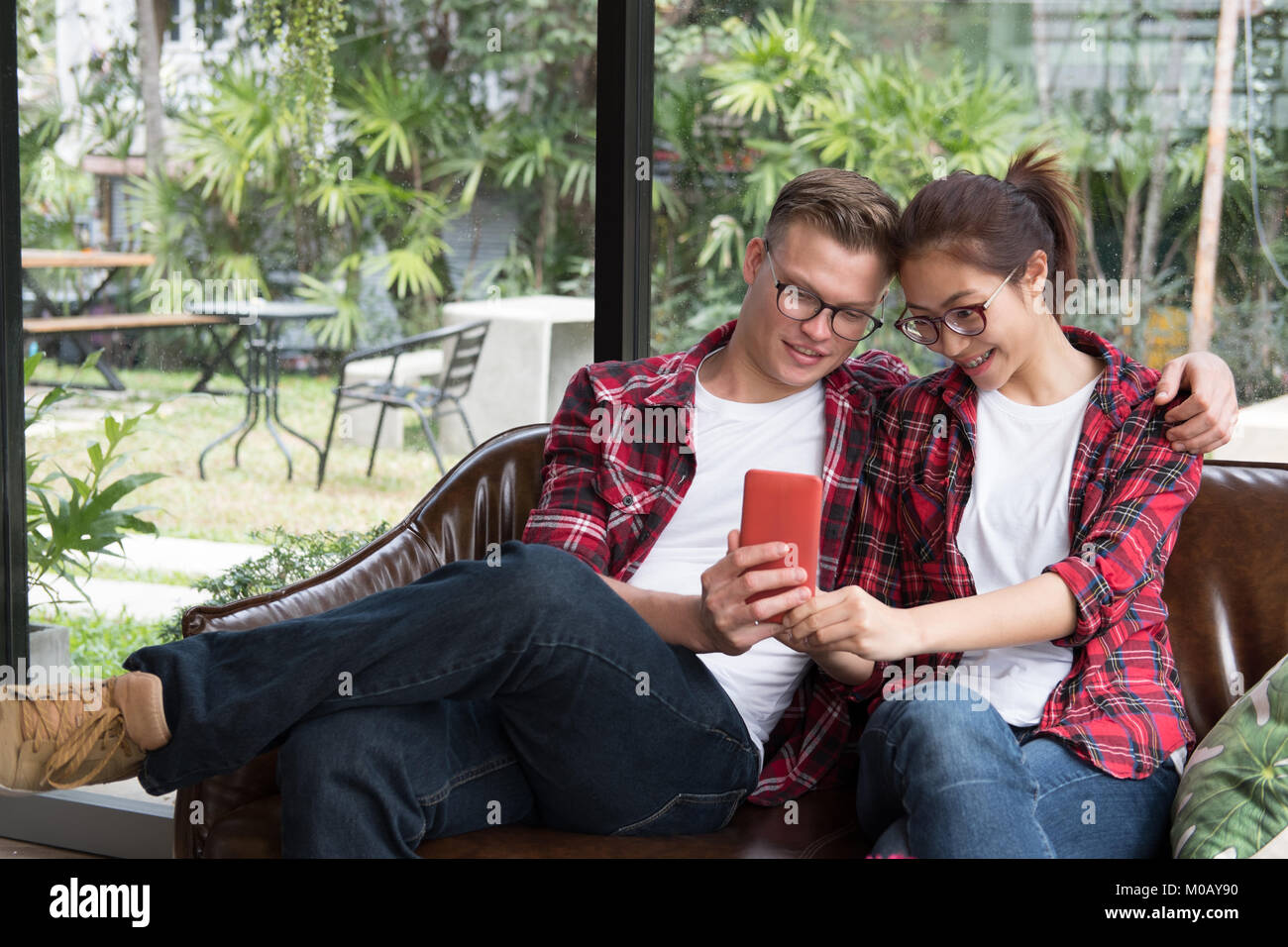 young couple in love smile & look at smart phone. caucasian man & asian ...
