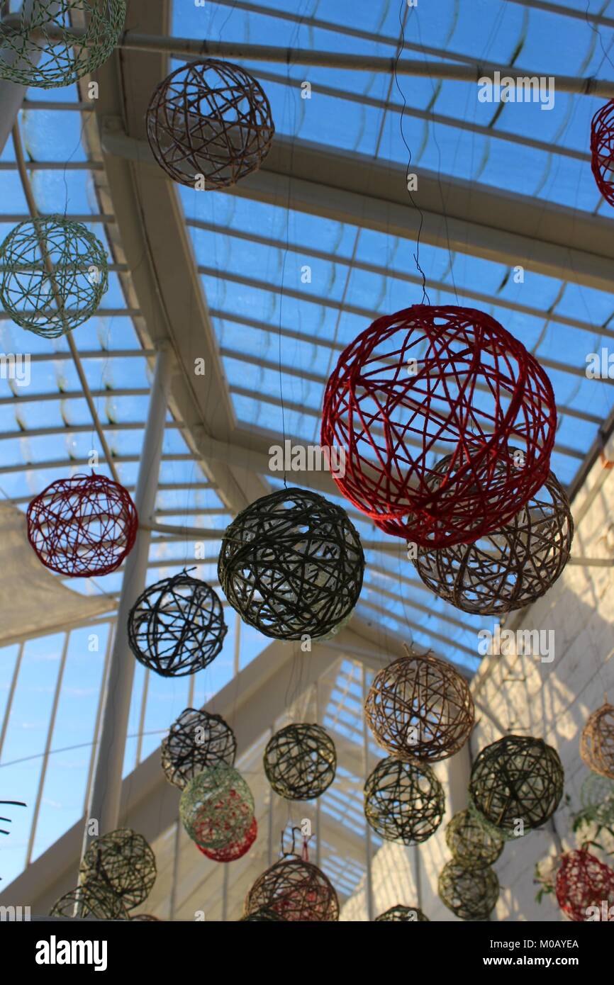 Looking up at large balls made of coloured raffia, hung from the roof ...