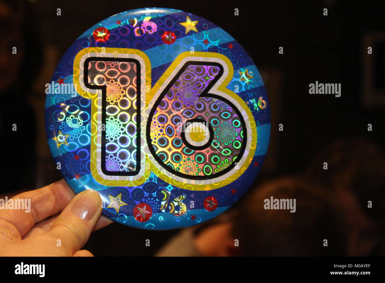 Large birthday badge showing number 16 with fluorescent colours held by ...