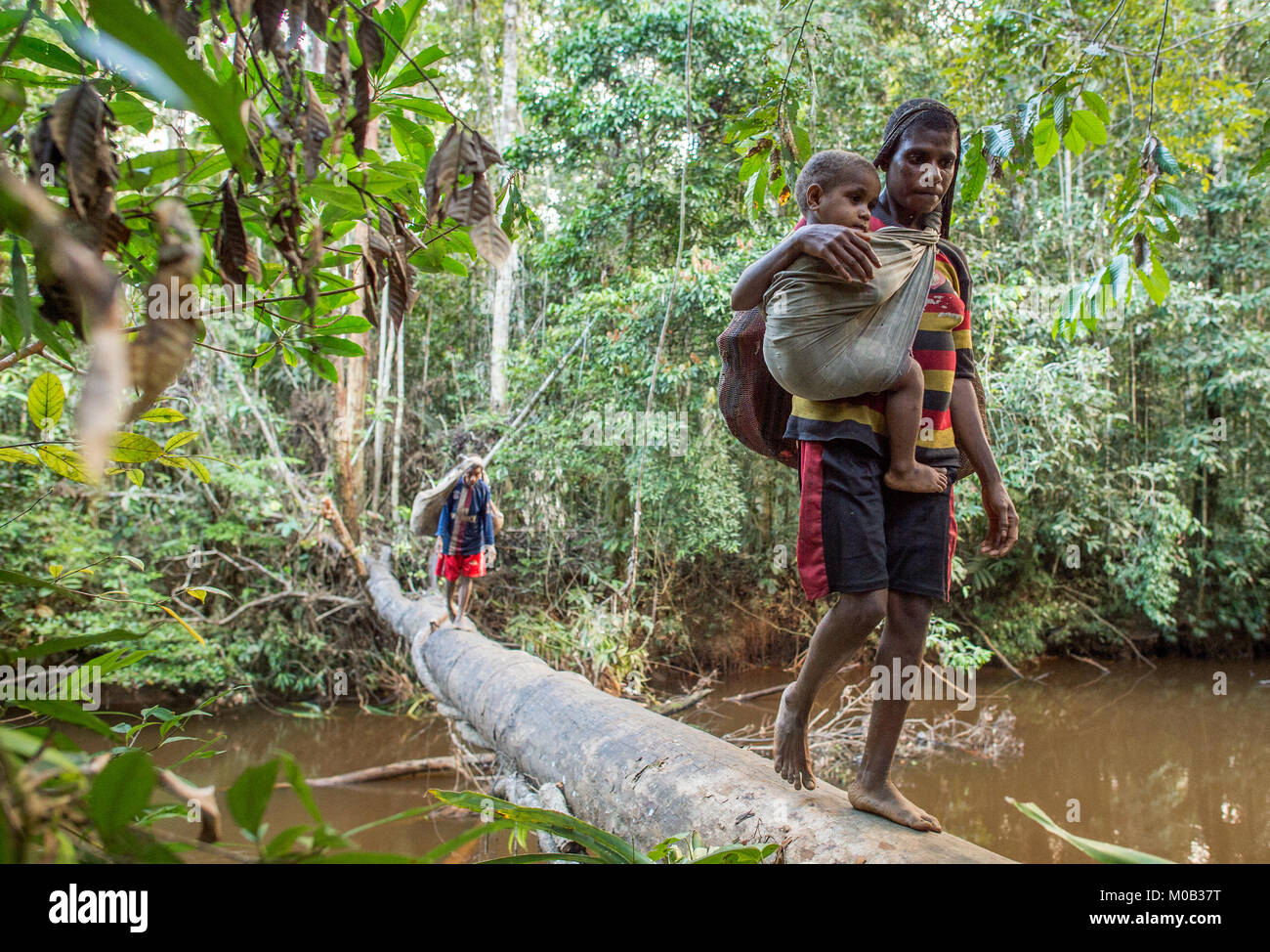 Woman with child crossing river on the tree trunk bridge, tribe of ...