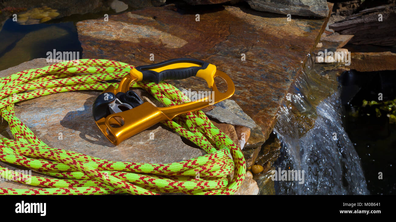 Climbing rope and an ascender on a rock near a small waterfall Stock ...