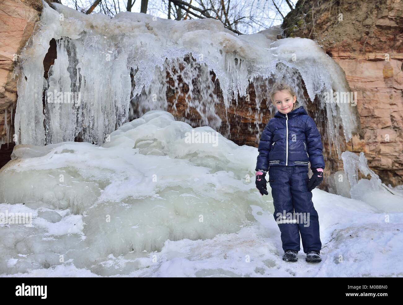 Smiling little girl posing near frozen waterfall, winter Stock Photo ...