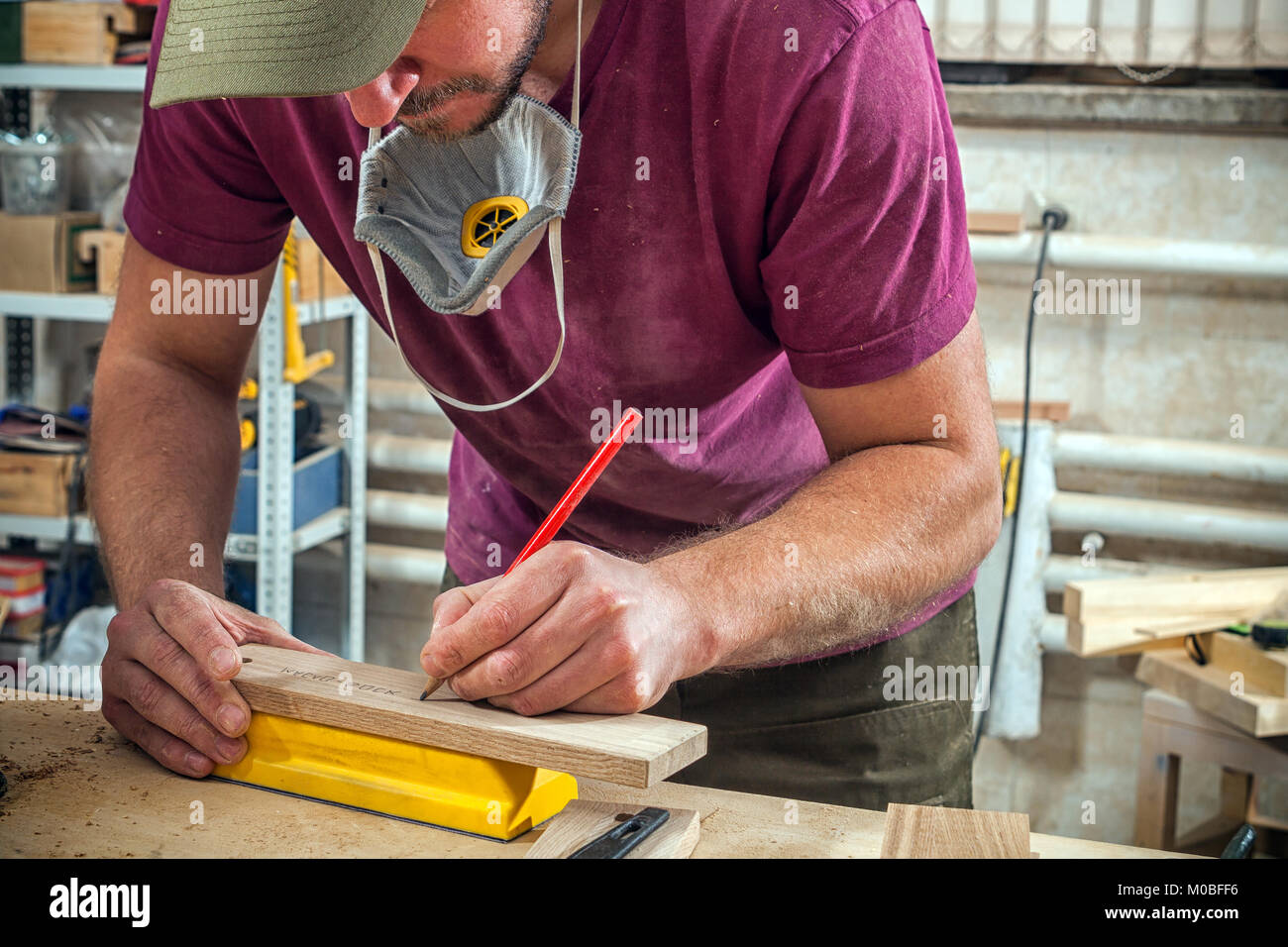 A young strong man builder carpenter works with a wooden bar for making ...