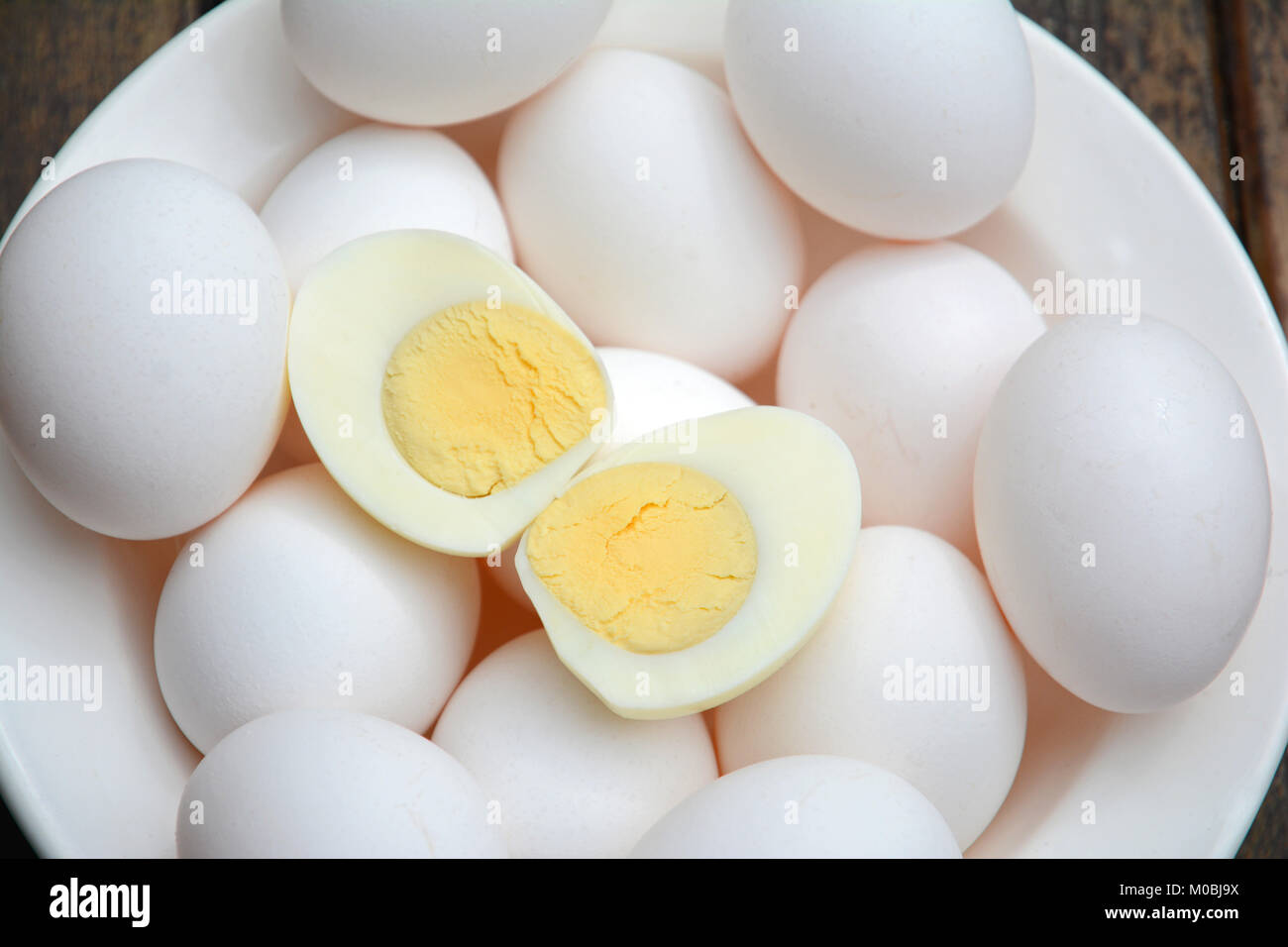 Numerous white hard boiled eggs in white bowl with two halves with ...