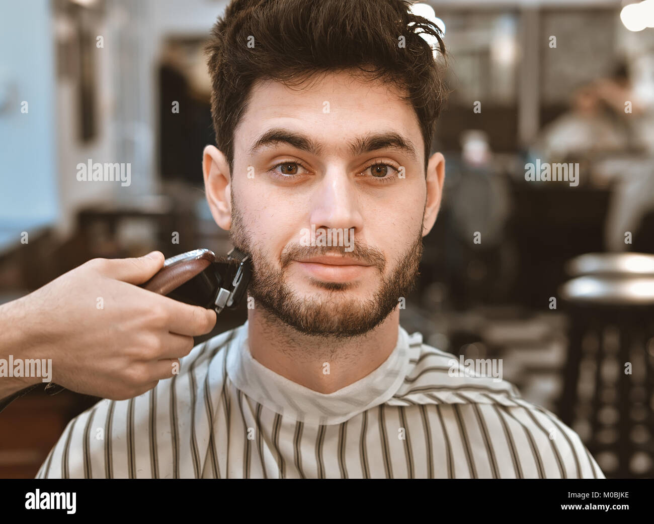 The hands of young barber making haircut to attractive man in ...