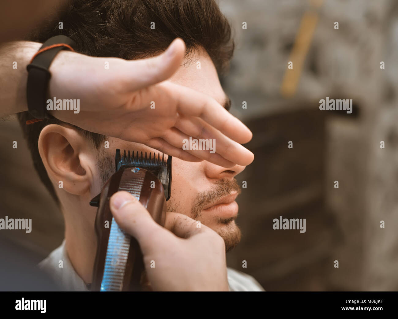 The hands of young barber making haircut to attractive man in ...