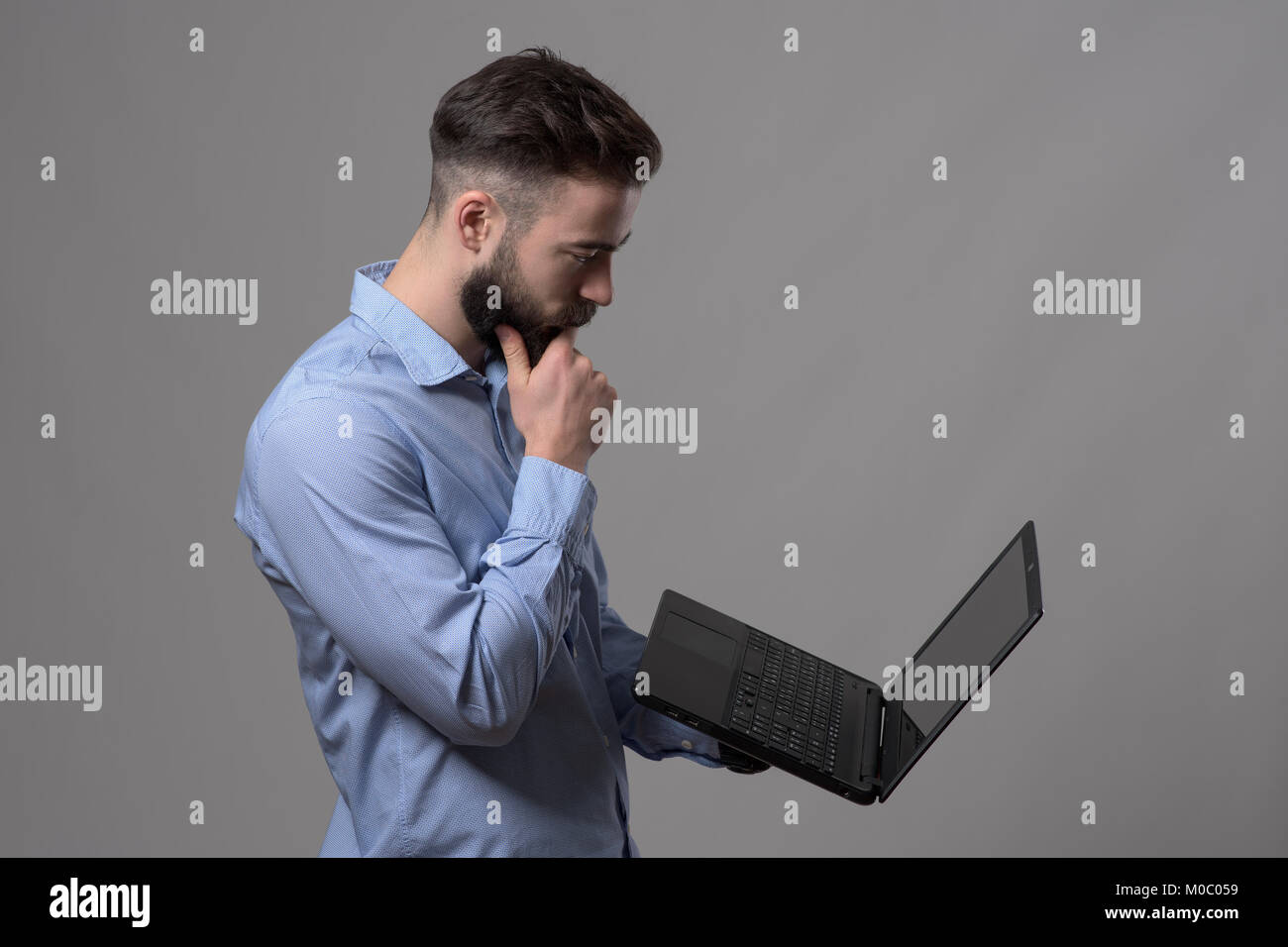 Serious young bearded business man looking at laptop computer and ...