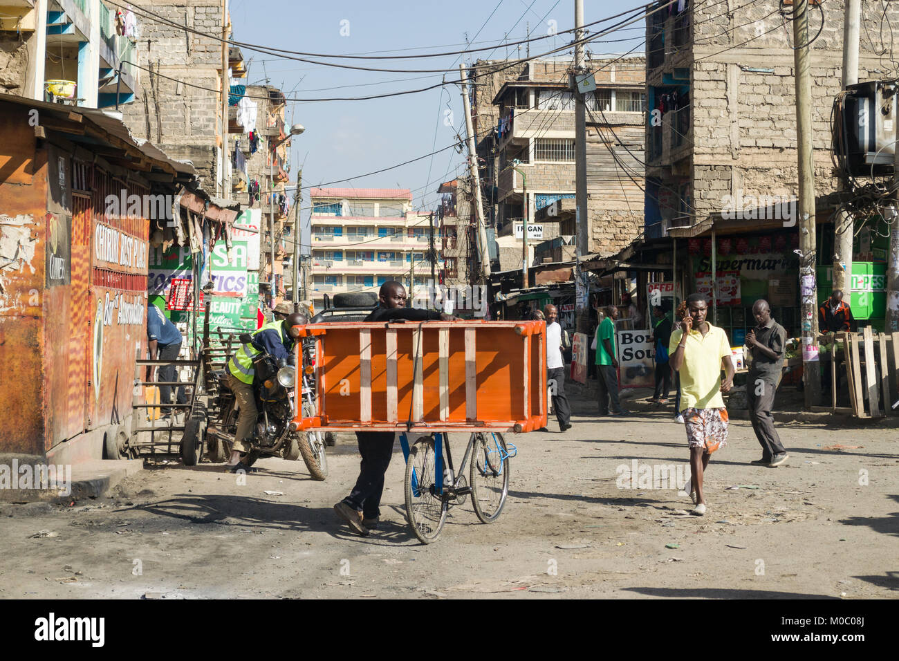 View down a road in Huruma, a man transports a small bed on the back of ...