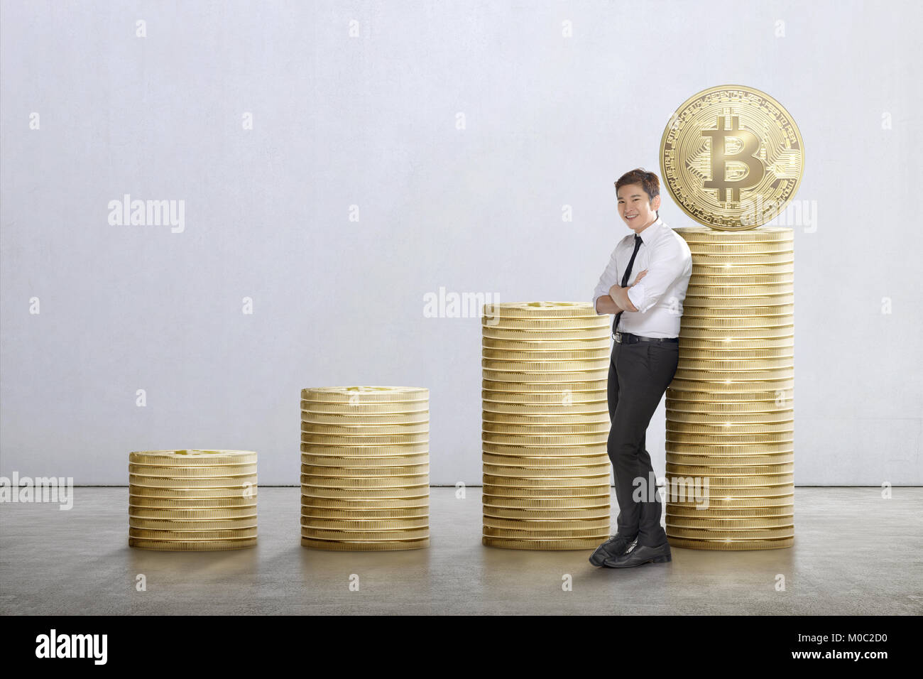 Young asian businessman lean back on bitcoins stack on grey wall ...