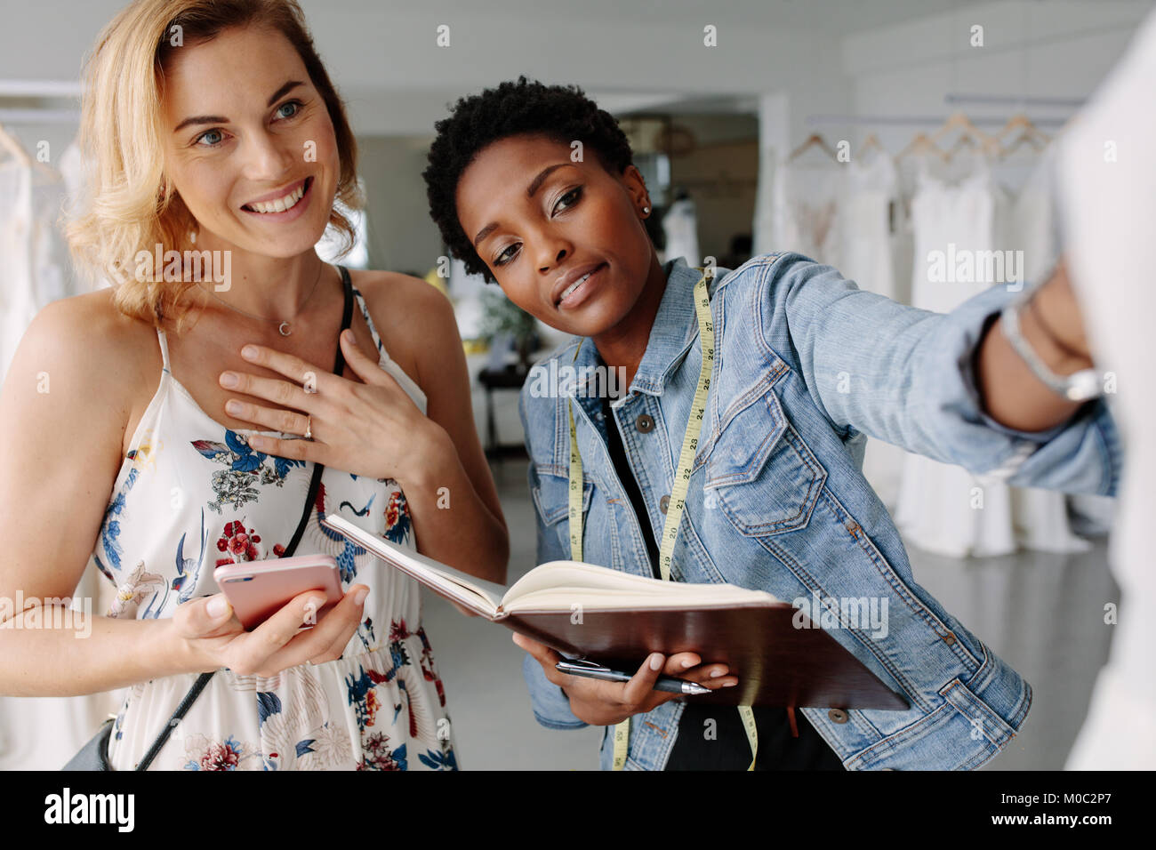 Wedding fashion shop owner helps the bride in choosing bridal dress ...