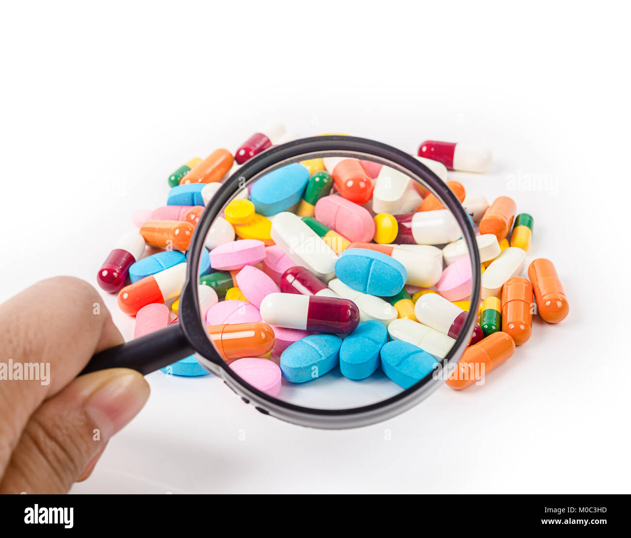 Hand holding magnifying glass with medicine pills on white background ...