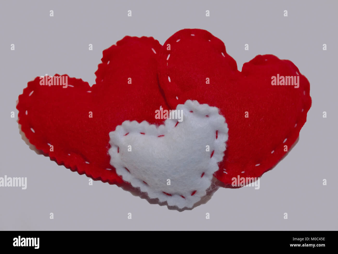 Three handmade cloth hearts, two larger red ones with a smaller white ...