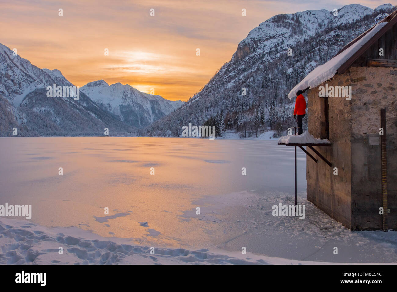Man standing on small balcony on house in frozen and snow covered lake ...