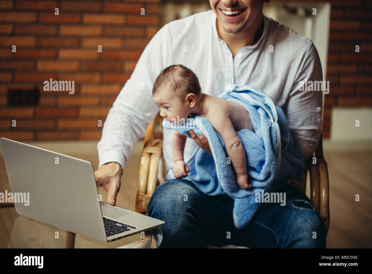 Father With Newborn Baby Working From Home Using Laptop Stock Photo - Alamy