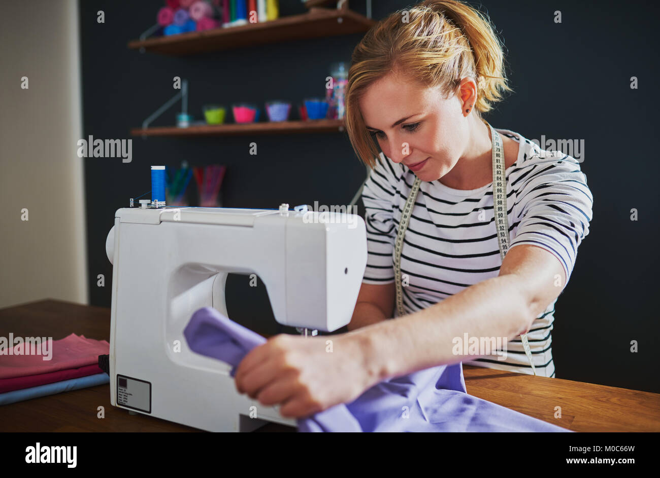 Young creative fashion designer using a sewing machine to stitch a ...