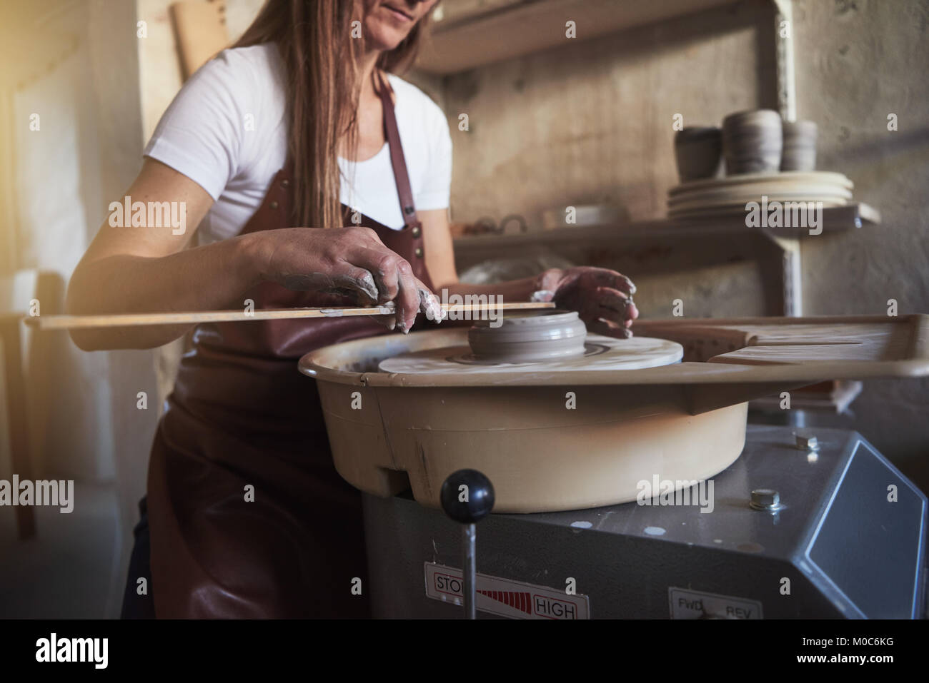Female artisan sitting in her ceramic workshop using a ruler to measure ...